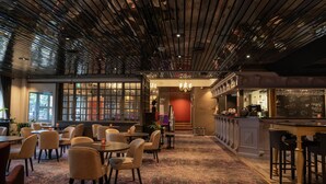 Um hall de hotel com mesas redondas, cadeiras, área de bar e uma escada que leva ao andar superior.
