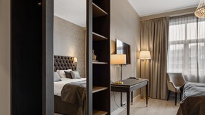 Quarto de hotel com cama, escrivaninha, cadeira, televisão e janela com cortinas.
