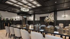 Uma sala de conferência com uma mesa comprida, cadeiras, um candelabro e uma lareira.