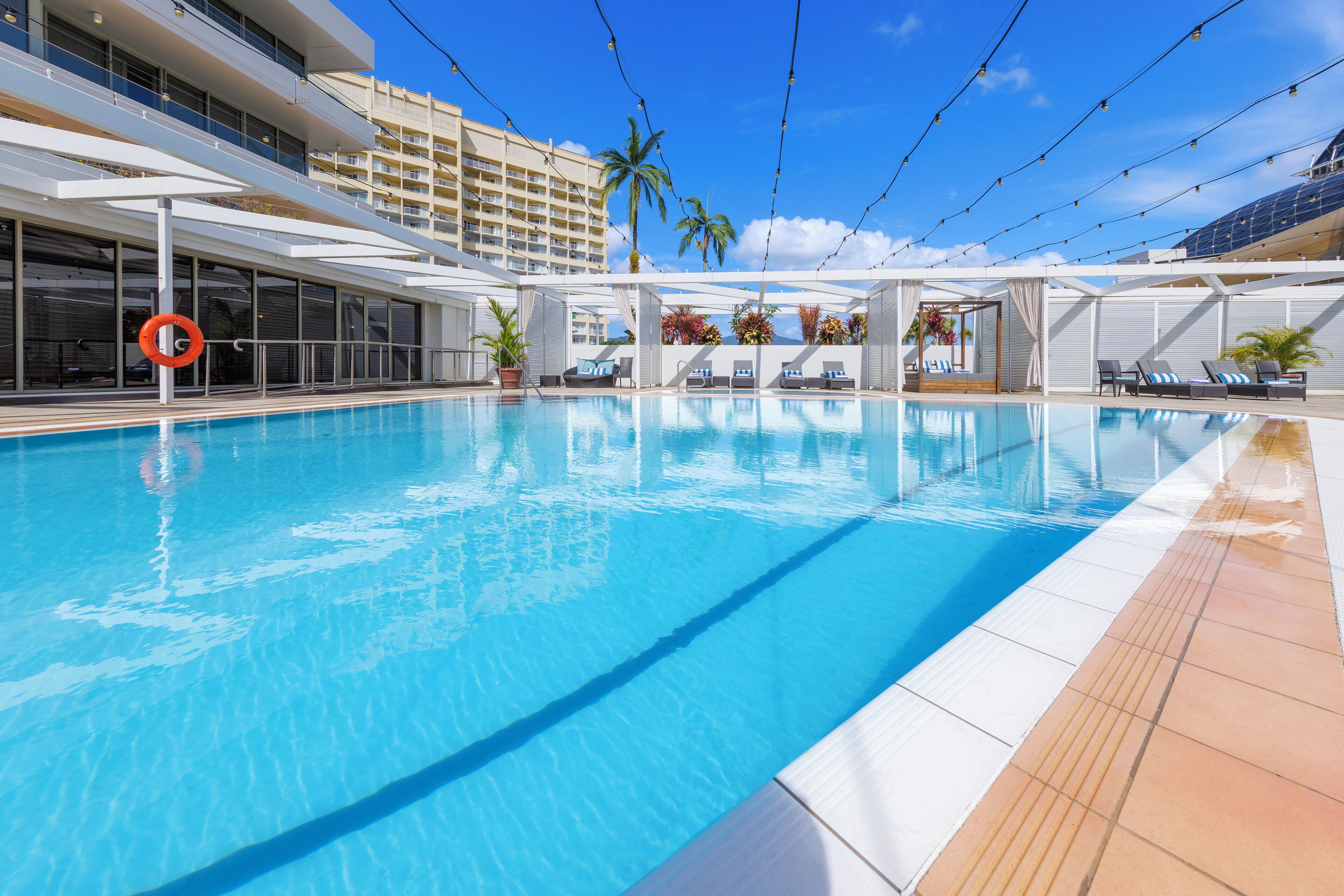 Piscina com água azul cristalina, rodeada por espreguiçadeiras e plantas em vasos.