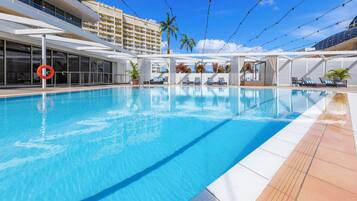 Piscina com água azul cristalina, rodeada por espreguiçadeiras e plantas em vasos.