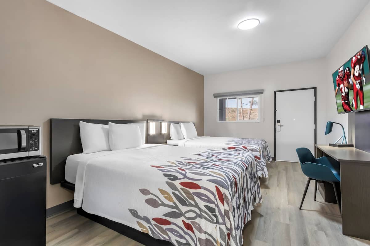 Quarto de hotel com cama, escrivaninha, cadeira, micro-ondas e janela.