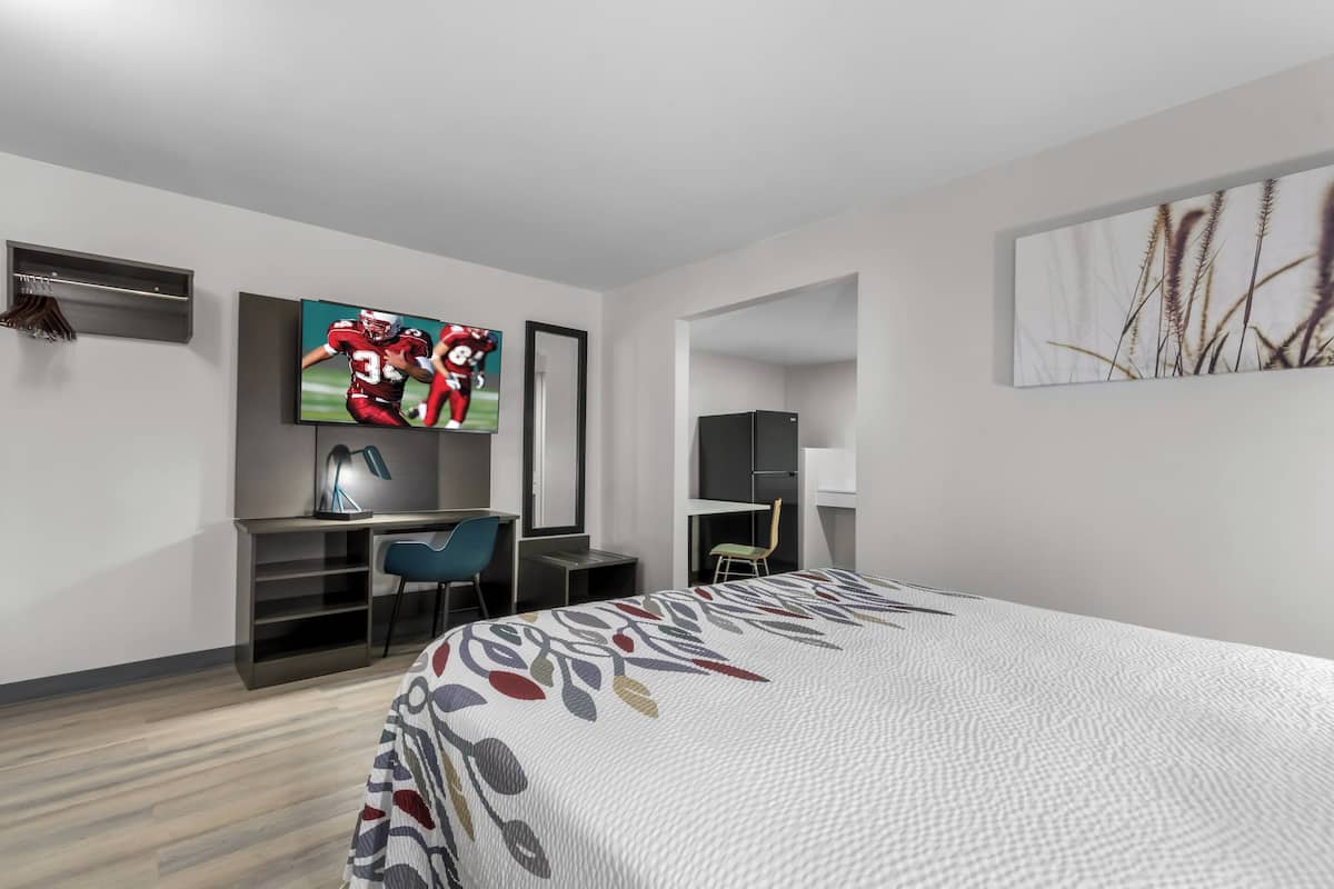 Quarto de hotel moderno com cama, escrivaninha, cadeira, televisão e guarda-roupa.