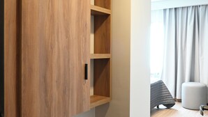 Quarto com guarda-roupa de madeira, sofá cinzento e janela com cortinas.