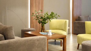 Um hall de hotel moderno com um painel de madeira decorativo, um abajur, uma mesa de centro com um vaso de plantas verdes e dois sofás.