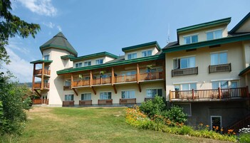 Hotel com vários andares, torre central, varandas e um jardim bem cuidado.