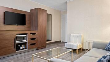Uma sala de estar moderna com televisão de tela plana, micro-ondas embutido, armário de madeira, mesa de centro de vidro, poltrona listrada e sofá.