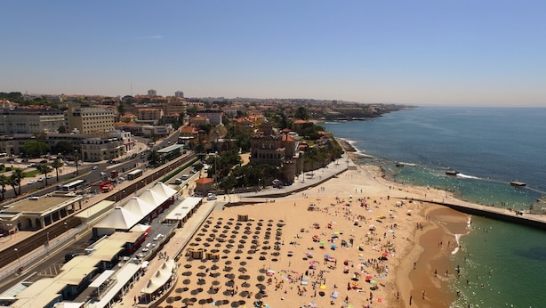 Paisagem costeira urbana com uma praia extensa, um calçadão e uma estação de trem.