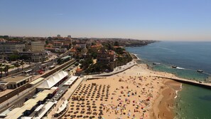 Paisagem costeira urbana com uma praia extensa, um calçadão e uma estação de trem.