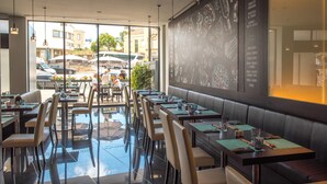 Um restaurante com decoração moderna, apresentando uma ampla área de jantar com cabines e mesas, um grande quadro negro com o menu e amplas janelas com vista para a rua.