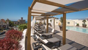 Área de piscina no terraço com espreguiçadeiras e guarda-sóis, com vista para a paisagem urbana e o mar.