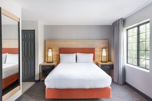 Quarto de hotel com uma cama grande, duas mesas de cabeceira com luminárias, um guarda-roupa e uma janela com cortinas.