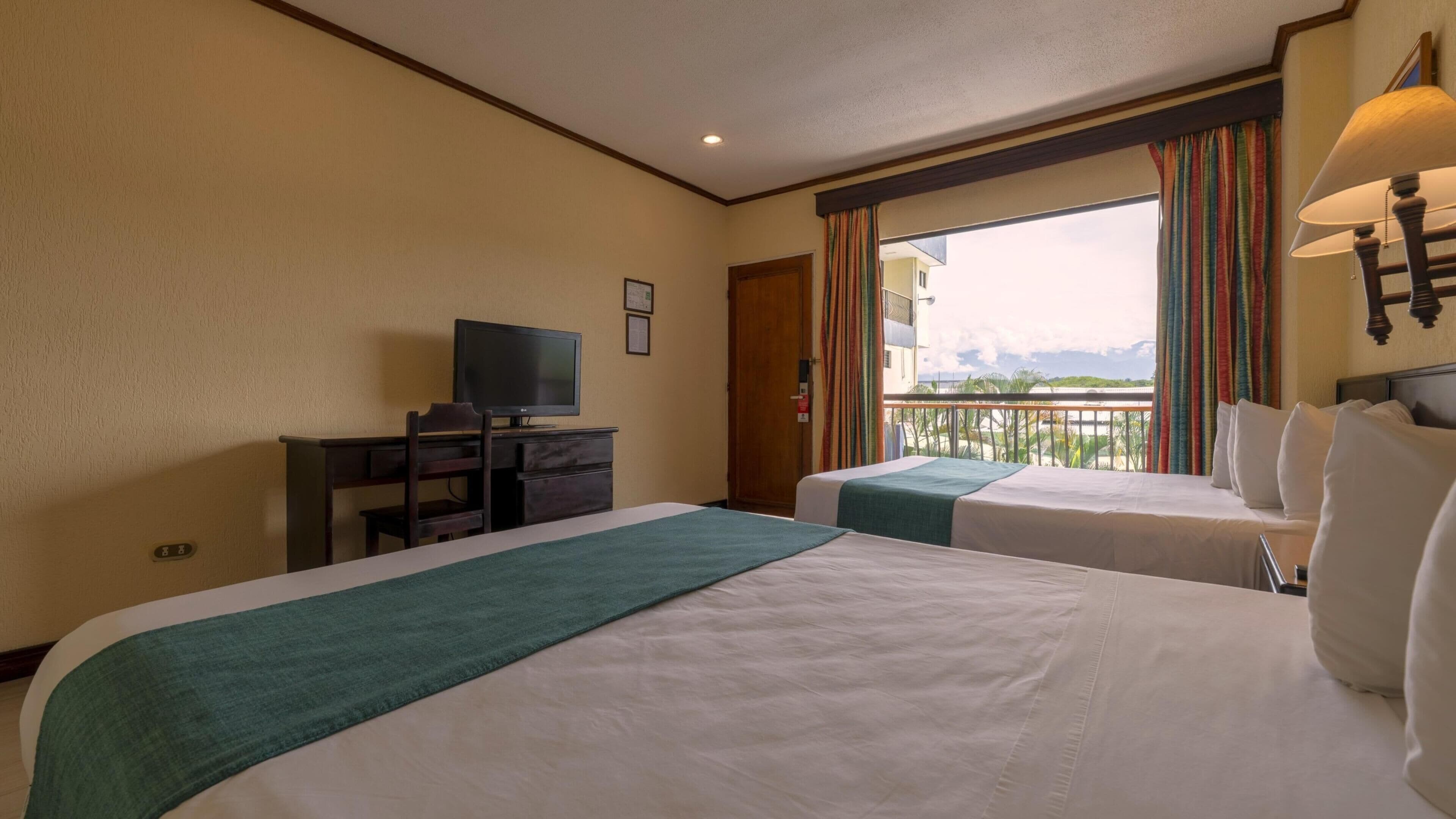 Quarto de hotel com duas camas, uma escrivaninha com televisão e vista para o exterior.