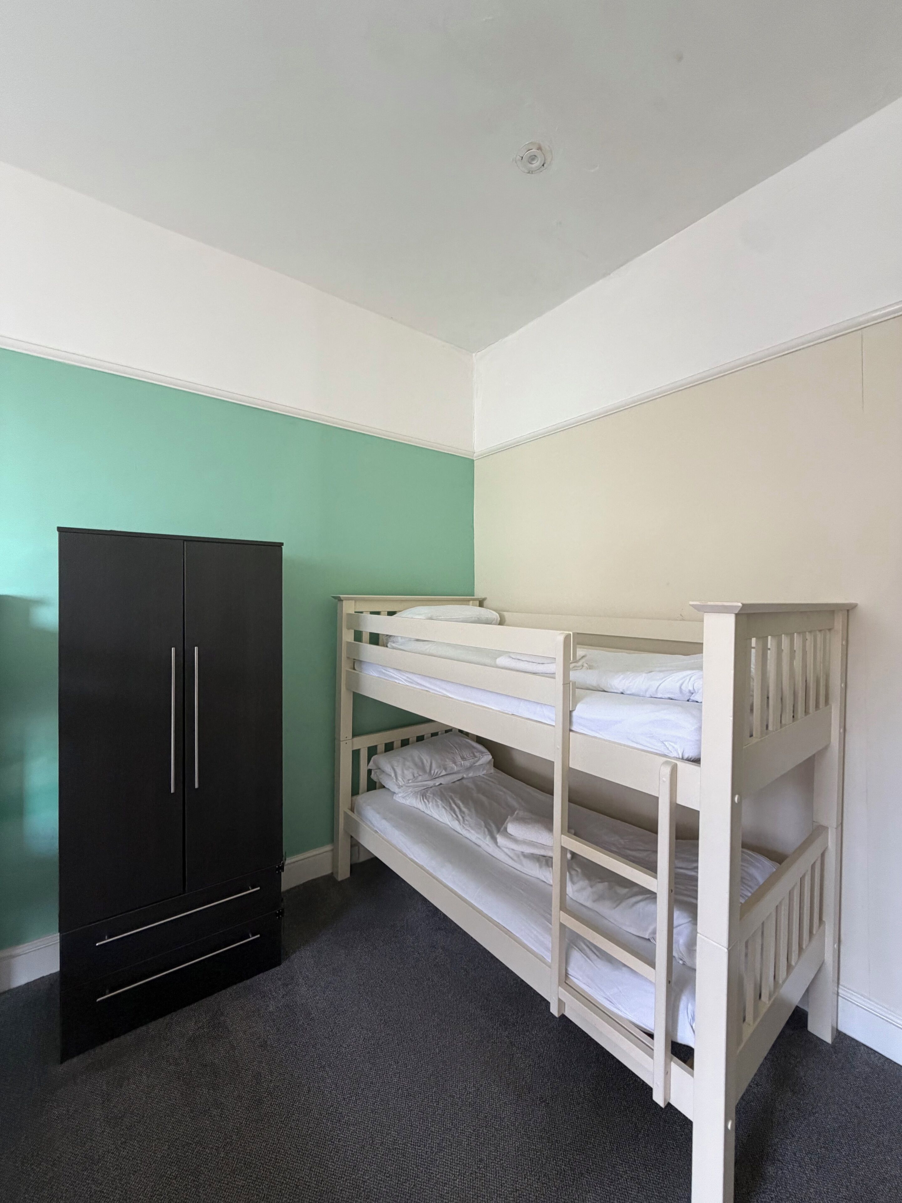 Quarto com cama beliche, guarda-roupa preto e parede verde.