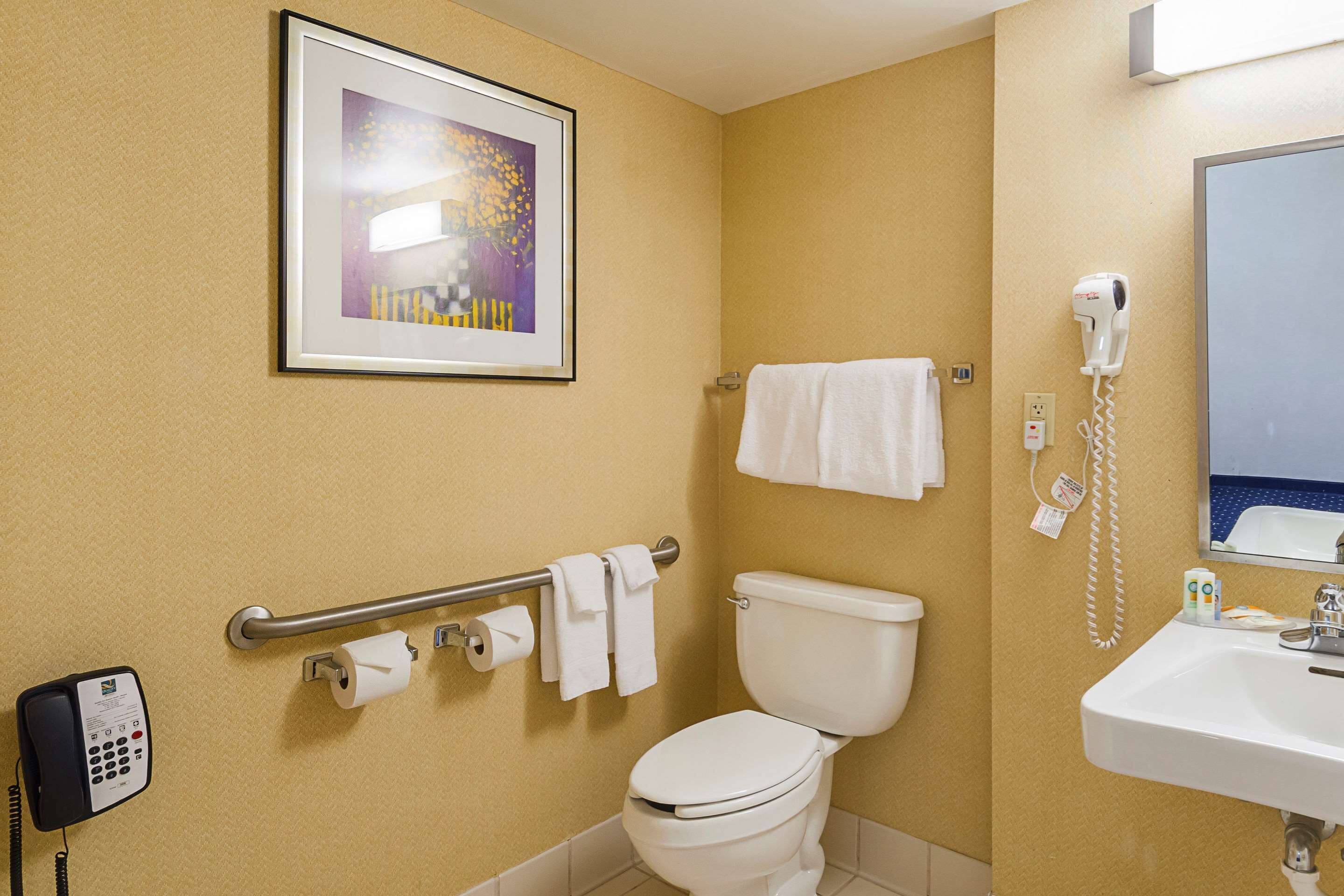 Um banheiro com vaso sanitário, secador de mãos, pia, quadro na parede e telefone.
