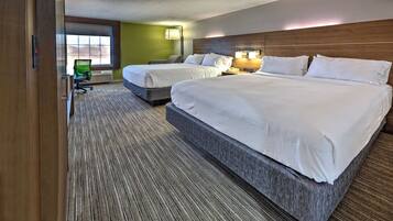 Quarto de hotel com duas camas, uma escrivaninha, uma cadeira, uma janela e um abajur.