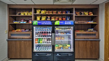 Duas máquinas automáticas identificadas como 'Holiday Inn Express Bebidas e Snacks Frios' e 'Holiday Inn Express Snacks Congelados', contendo diversas bebidas e petiscos.
