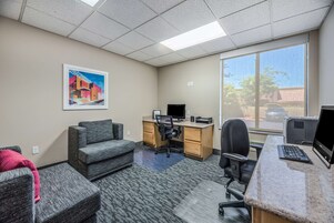Um espaço de escritório moderno com uma janela grande, uma mesa com computador, uma cadeira e um sofá.