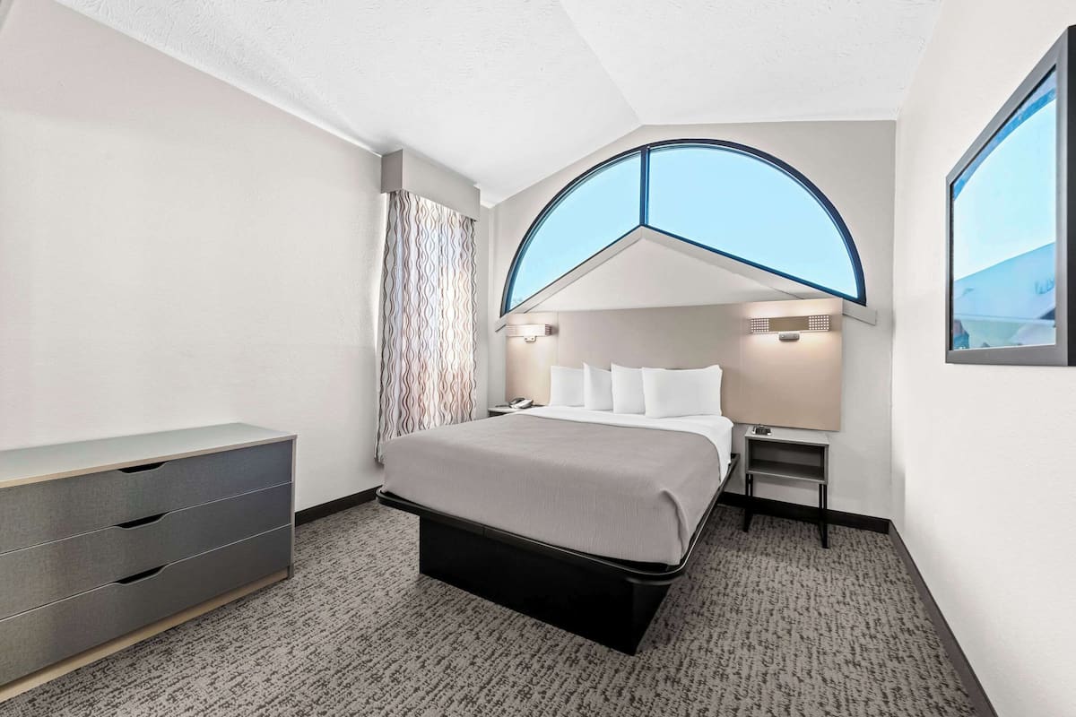 Quarto de hotel moderno com uma cama, cômoda, mesa de cabeceira e uma janela grande.