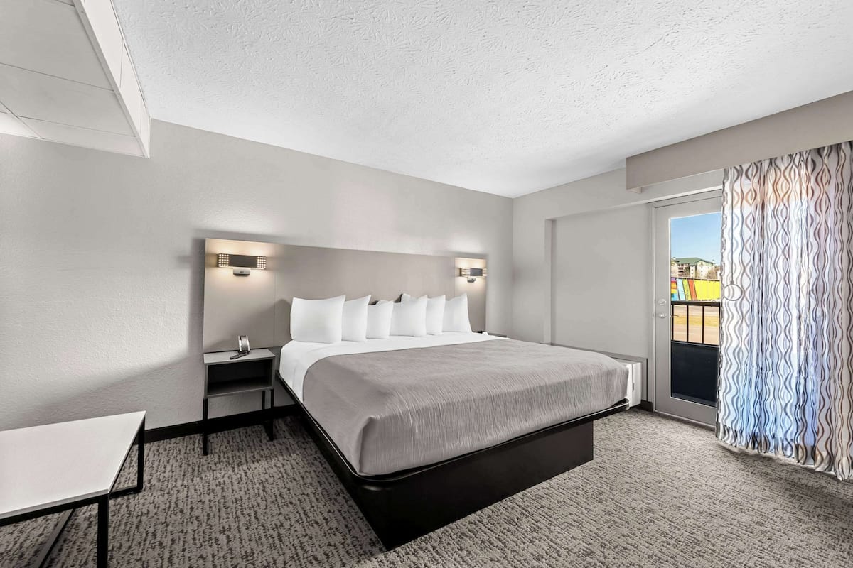 Quarto de hotel com uma cama grande, uma mesa de cabeceira e vista para o exterior por uma porta deslizante.