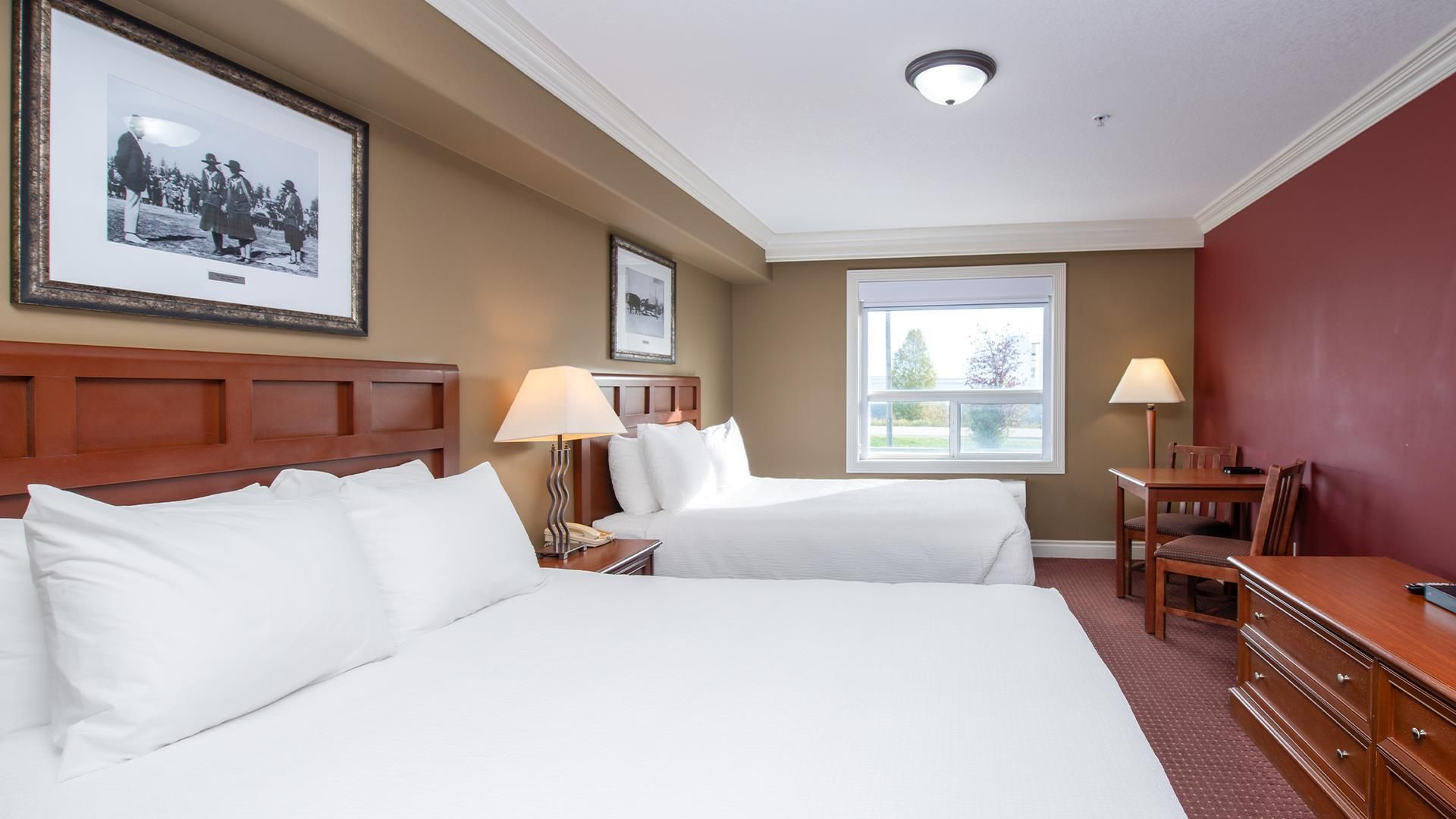 Quarto de hotel com duas camas, uma escrivaninha e uma janela com vista.
