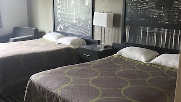 Quarto de hotel com duas camas, uma escrivaninha, uma cadeira e uma grande janela com vista para a cidade.