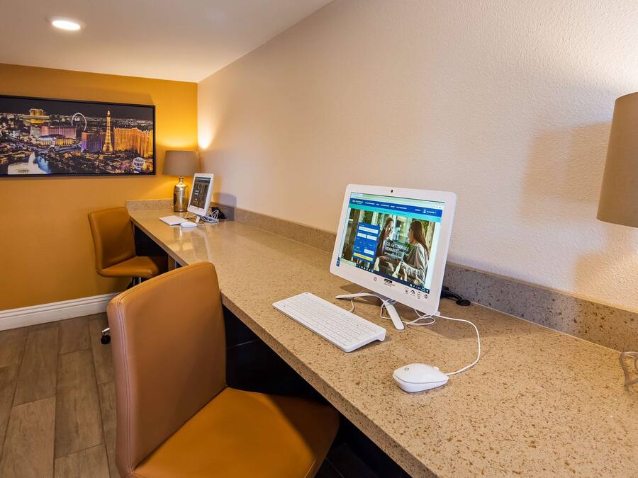 Quarto de hotel com escrivaninha, computador, luminária e uma cadeira.