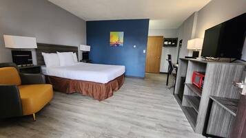 Quarto de hotel com uma cama, escrivaninha, cadeira, televisão e micro-ondas.