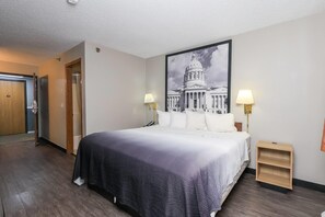 Quarto de hotel com uma cama grande, duas luminárias de cabeceira, um quadro de um edifício e uma mesinha de cabeceira de madeira.