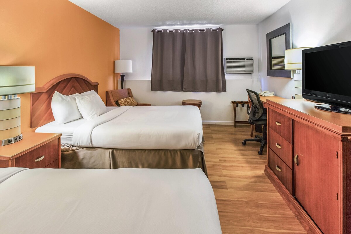 Quarto de hotel com duas camas, cómoda de madeira, televisão e secretária com cadeira.