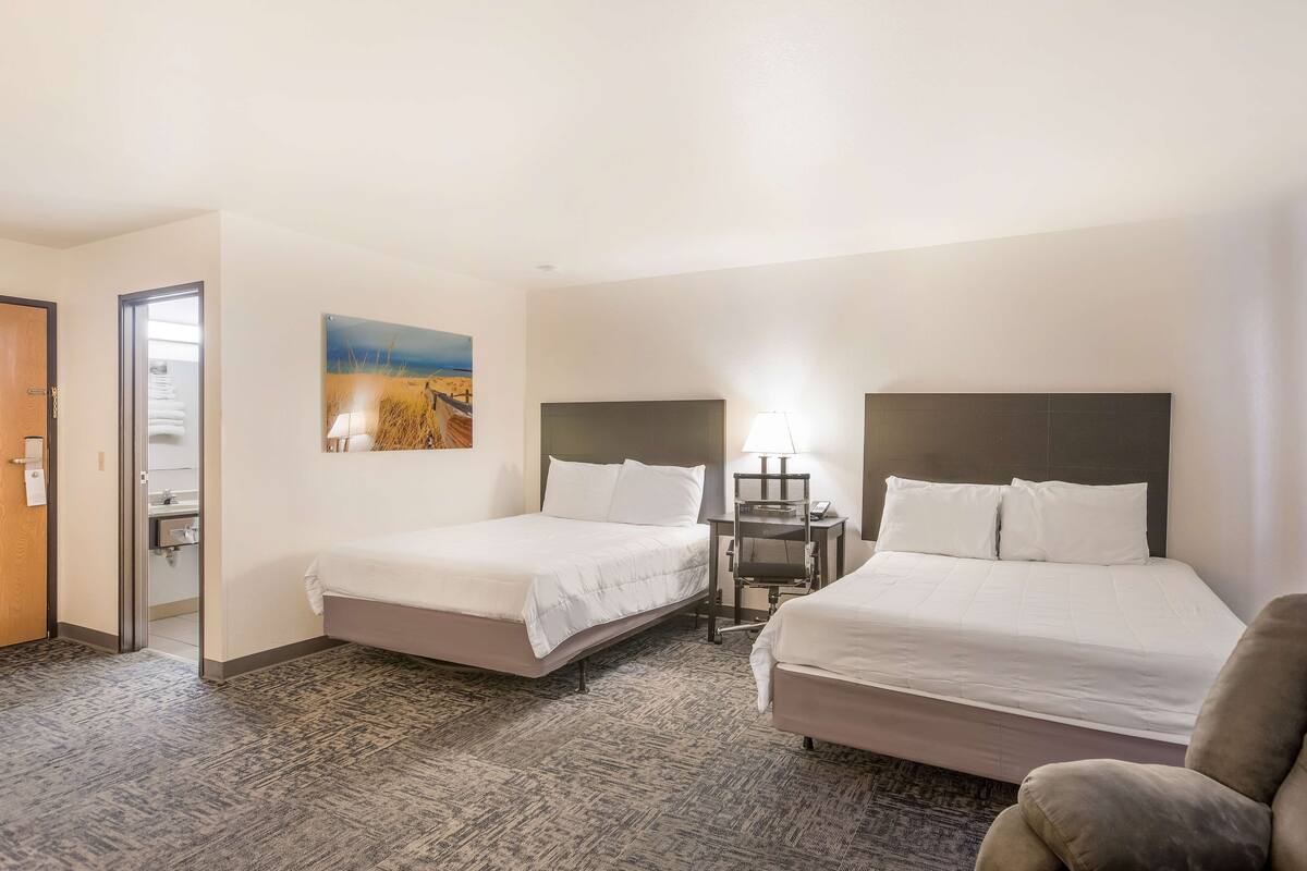 Quarto de hotel com duas camas, mesa de cabeceira, luminária e um quadro na parede.
