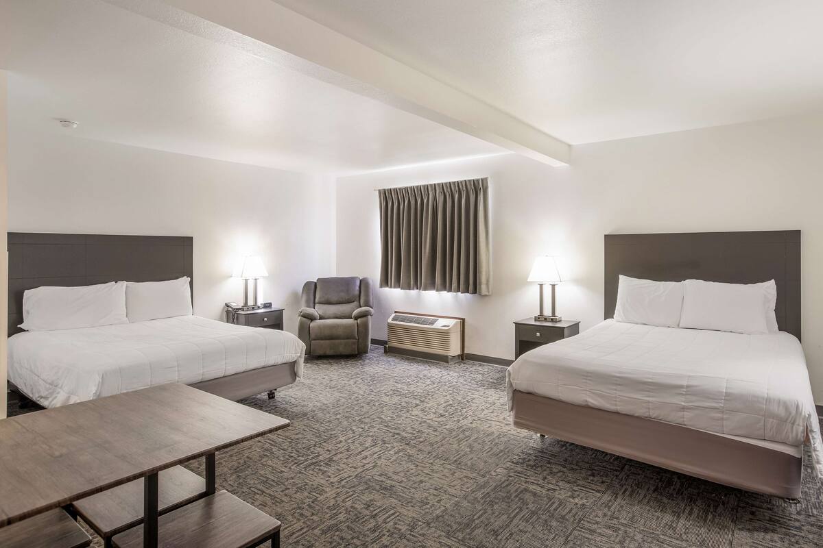 Quarto de hotel com duas camas, uma escrivaninha, uma cadeira, uma janela com cortinas e um aquecedor fixado na parede.