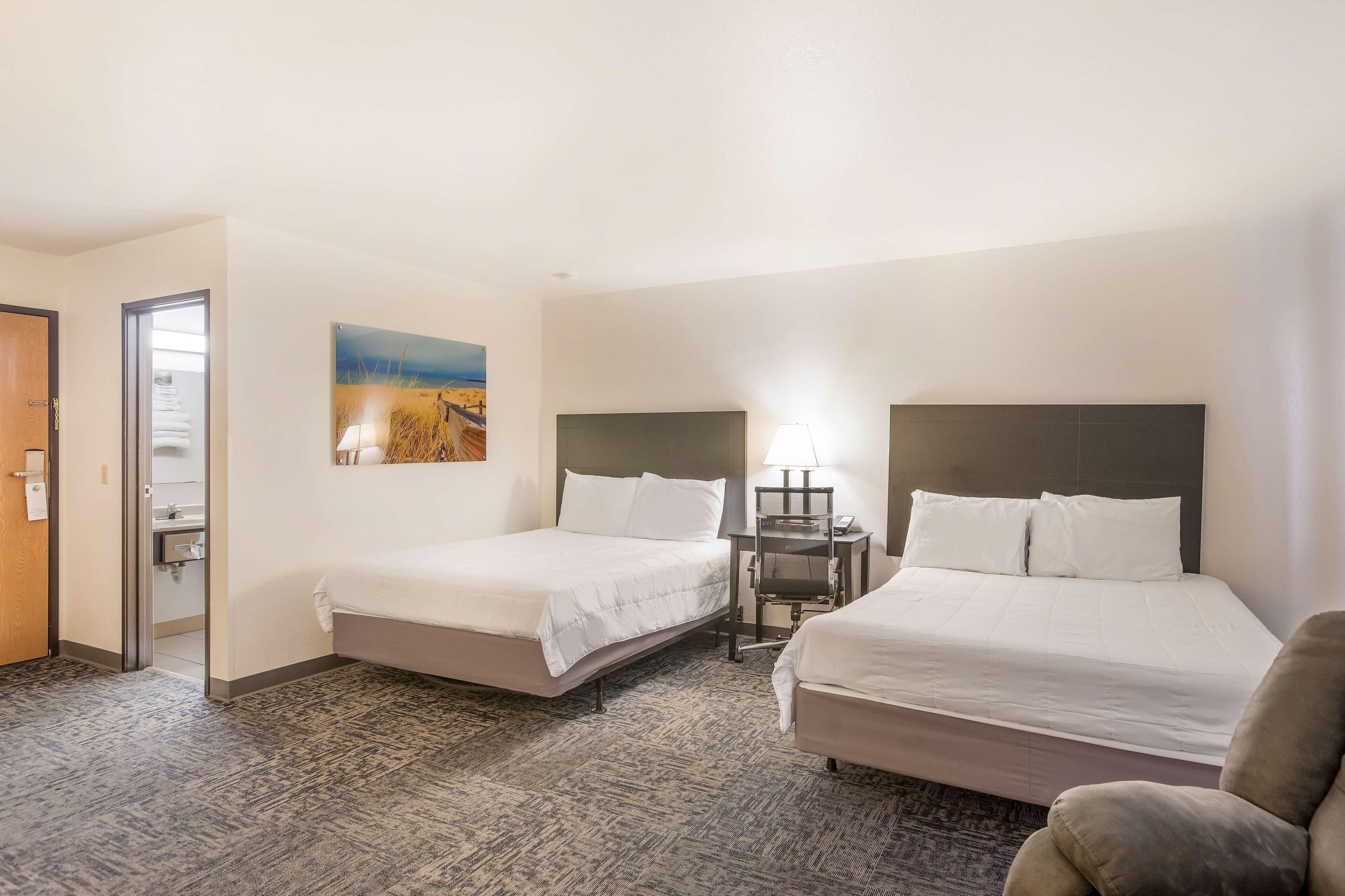 Quarto de hotel com duas camas, uma mesa de cabeceira, um abajur e um quadro na parede.
