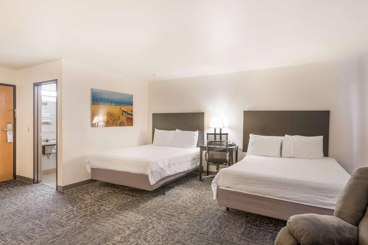 Quarto de hotel com duas camas, uma mesa de cabeceira, um abajur e um quadro na parede.
