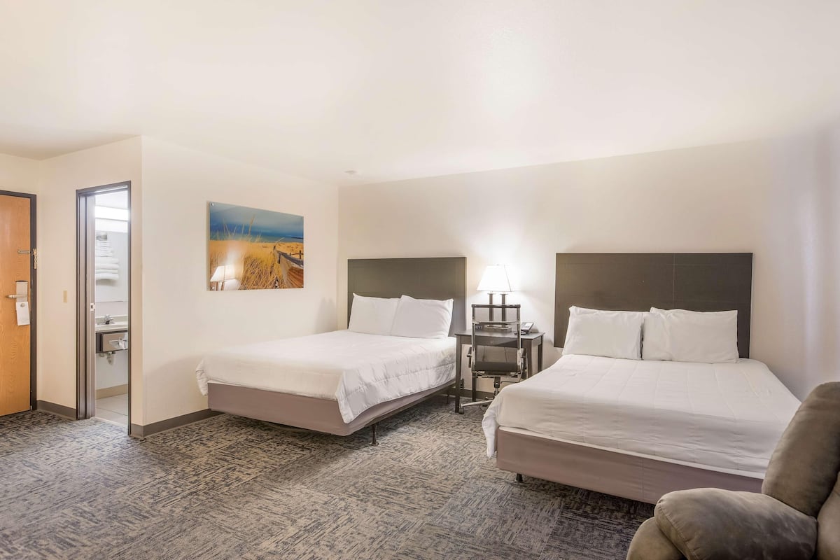 Quarto de hotel com duas camas, uma mesa de cabeceira, um abajur e um quadro na parede.