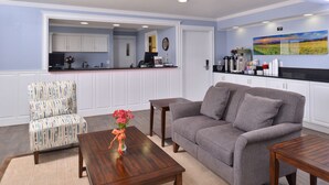 Uma sala de estar com um sofá cinzento, uma poltrona estampada e uma mesa de centro de madeira com um vaso de flores.