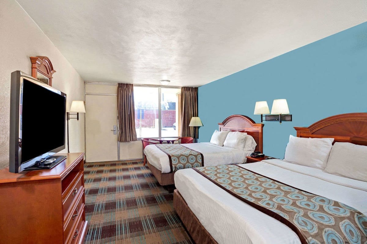 Quarto de hotel com duas camas, televisão, escrivaninha e janela com cortinas.