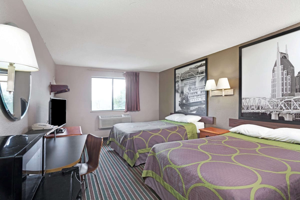 Quarto de hotel com duas camas, uma escrivaninha, uma cadeira, uma janela com cortinas e uma grande imagem da paisagem urbana na parede.