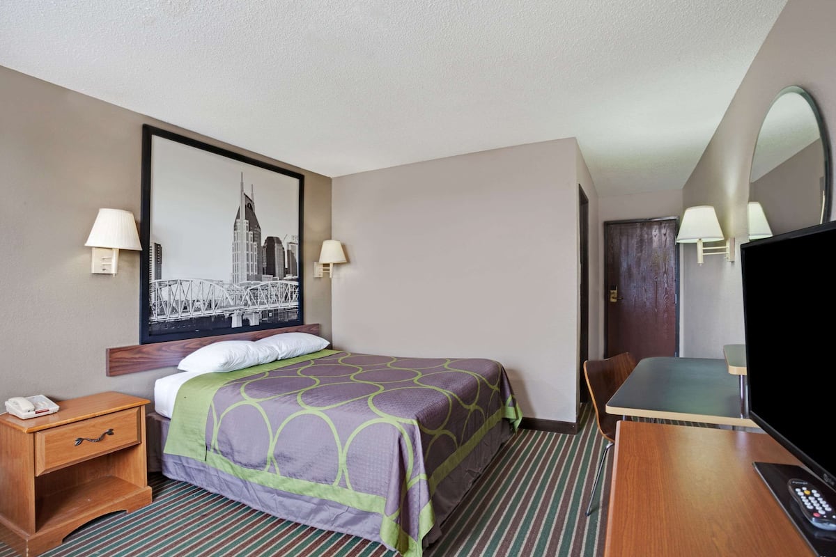 Quarto de hotel com cama, escrivaninha, televisão e porta.