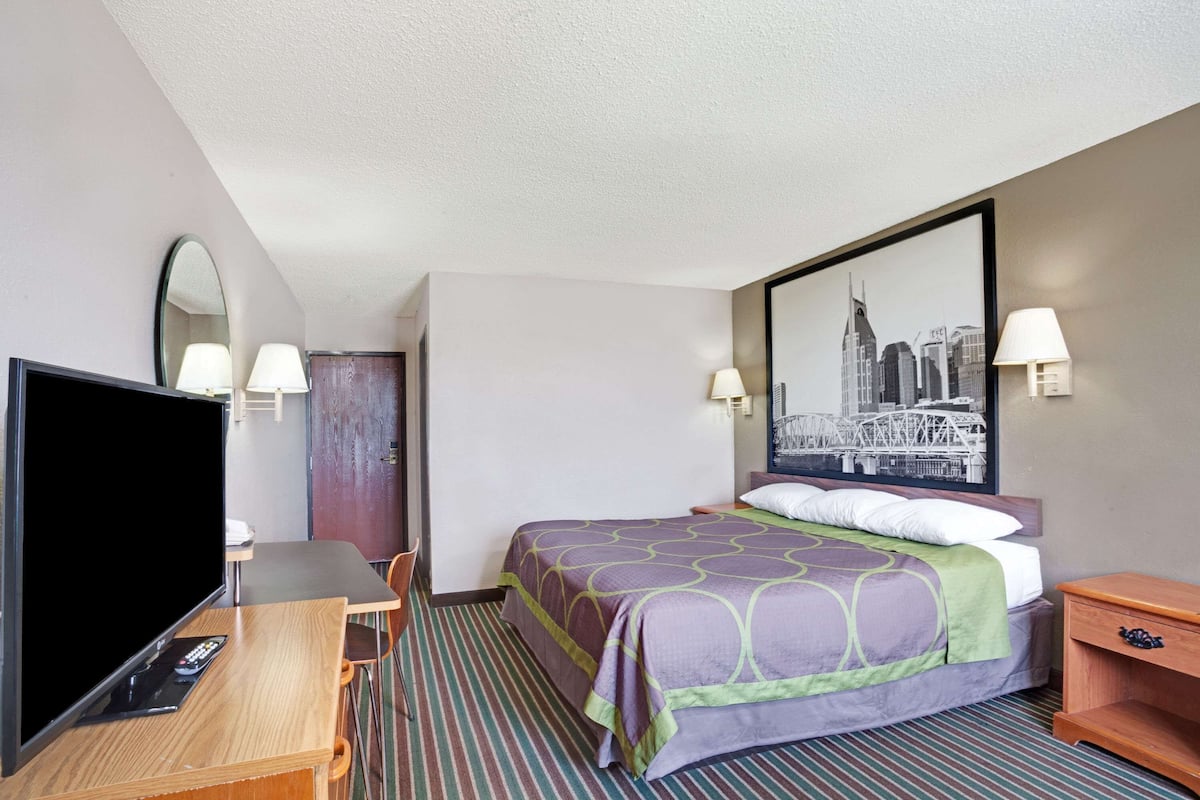 Quarto de hotel com cama, televisão, escrivaninha e cadeira.
