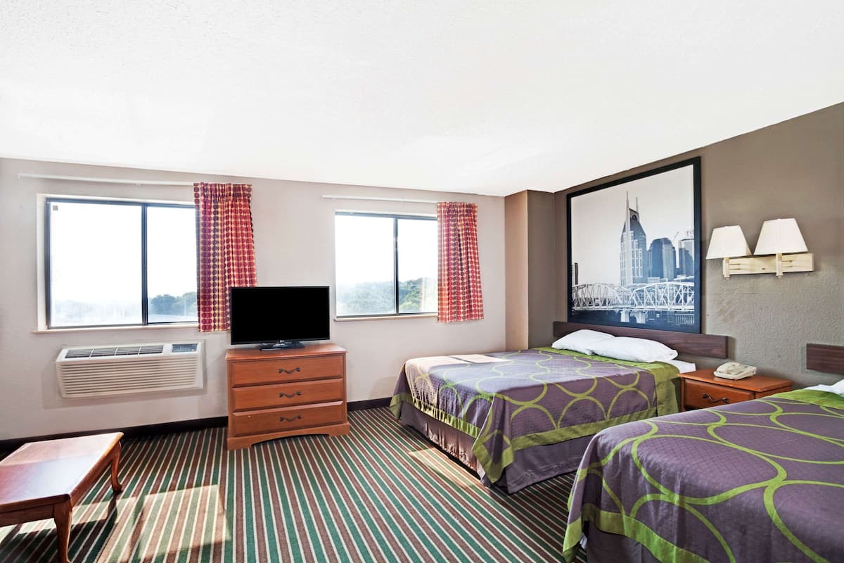 Quarto de hotel com duas camas, televisão, secretária e janela com cortinas.