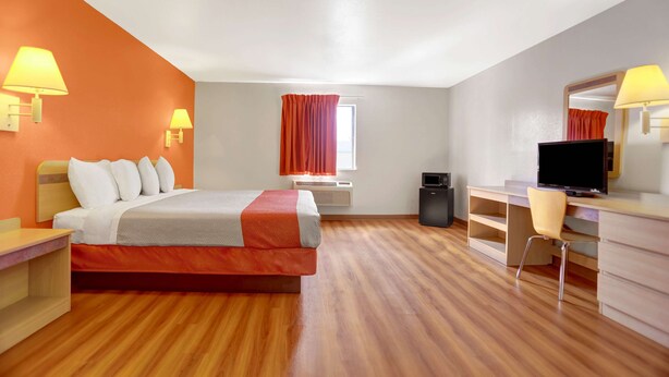 Quarto de hotel com cama, escrivaninha, cadeira, televisão e janela com cortinas.