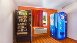 Quarto com máquina de vendas de lanches, uma grande máquina de Pepsi e uma janela com cortinas vermelhas.