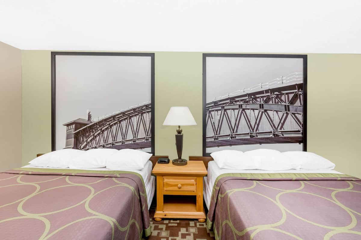 Quarto de hotel com duas camas, uma mesa de cabeceira com abajur e uma grande moldura com uma foto de uma ponte na parede.