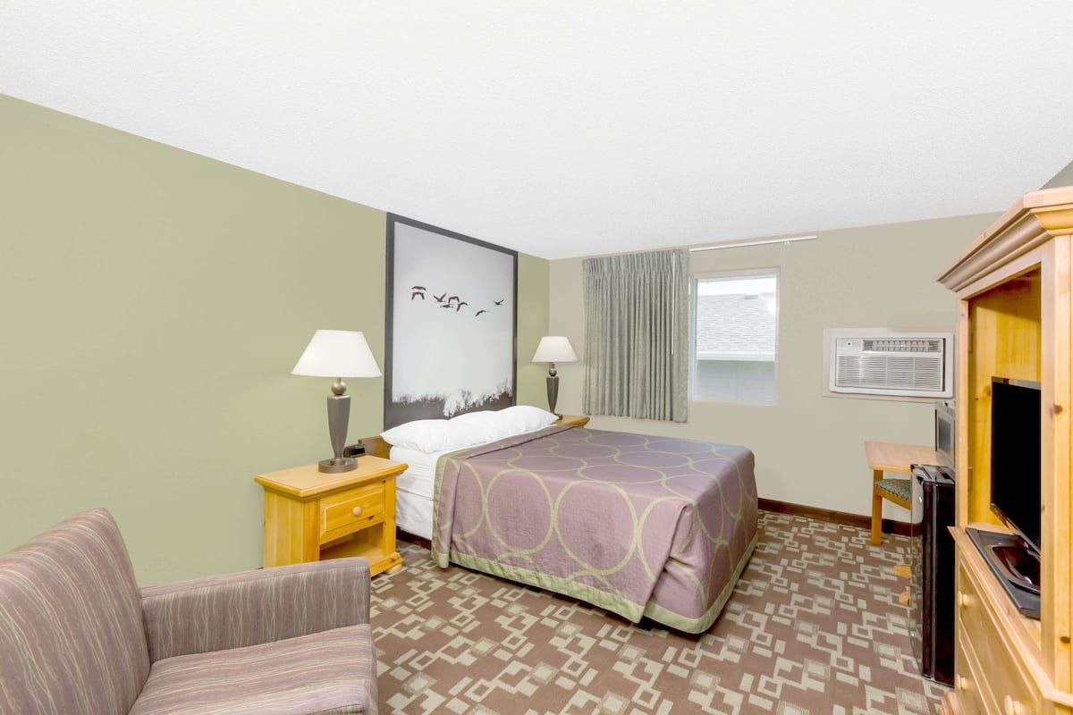 Quarto de hotel com cama, escrivaninha, cadeira, televisão e janela com cortinas.