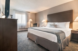 Quarto de hotel com cama grande, duas mesas de cabeceira, escrivaninha e janela com cortinas.