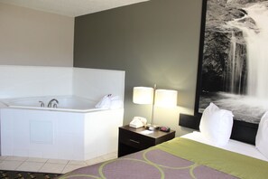 Quarto de hotel com uma banheira grande, uma mesa de cabeceira com abajur e uma TV na parede exibindo uma cena de cachoeira.