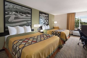 Quarto de hotel com duas camas, pinturas de paisagens amplas, uma mesa com cadeira e uma janela grande com cortinas.