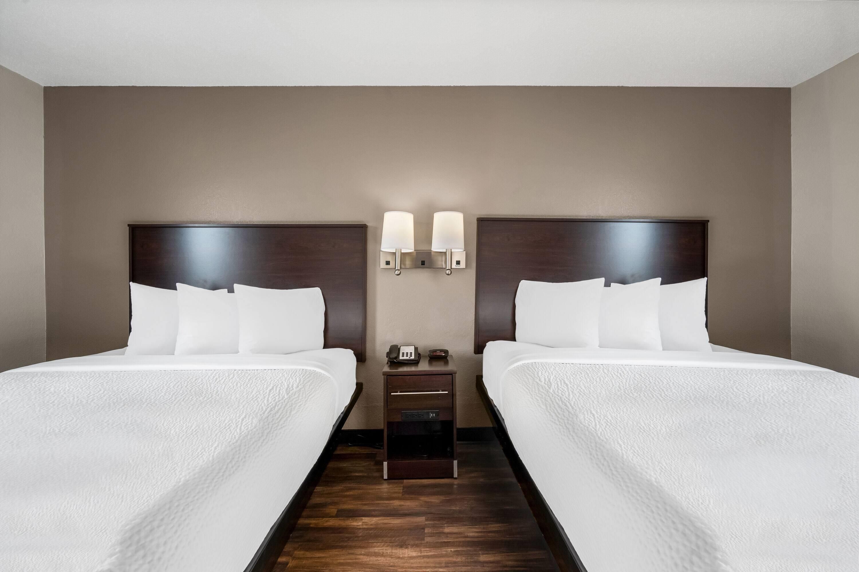 Quarto de hotel com duas camas, uma mesa de cabeceira com telefone e uma luminária na parede.