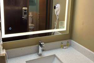 Um banheiro com uma pia moderna, um secador de cabelo fixado na parede e artigos de higiene pessoal no balcão.